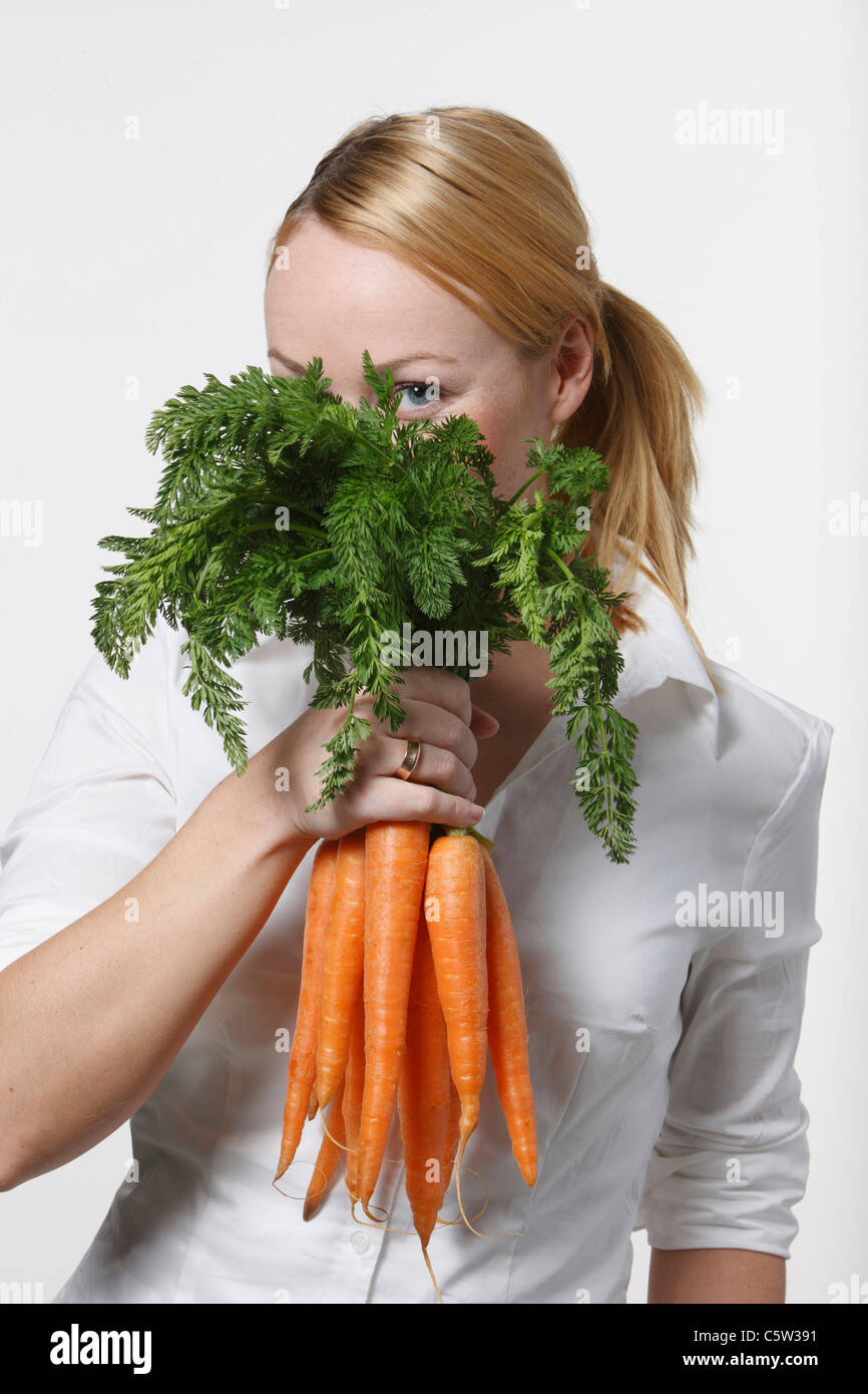 Young woman holding bunch of carrots, covering face, portrait Stock ...
