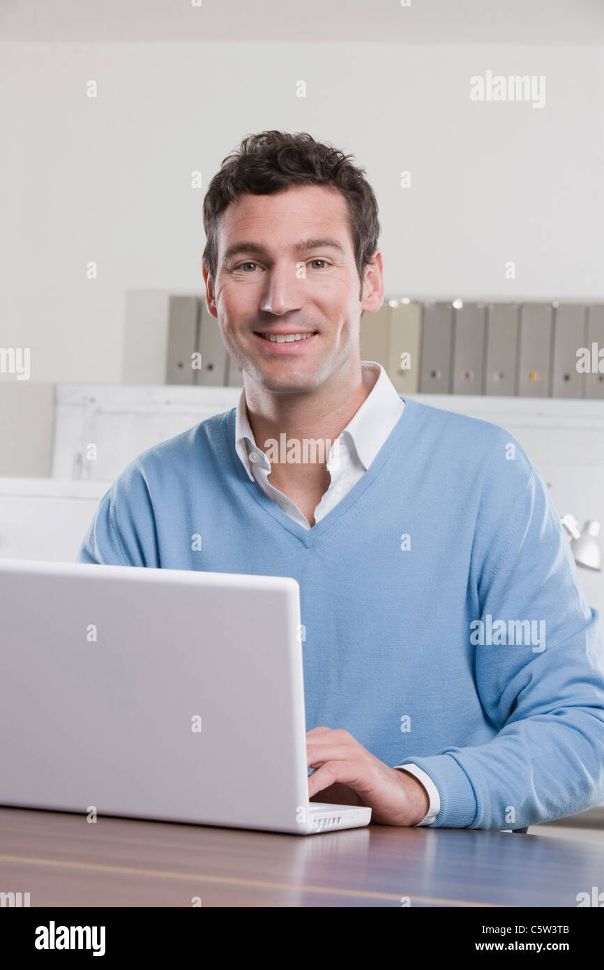 Germany, Munich, business man in office using laptop, smiling, portrait ...