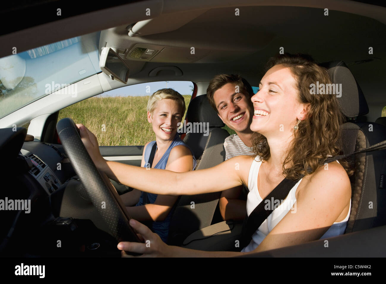 Germany, Bavaria, Young people riding a car, laughing, side view ...