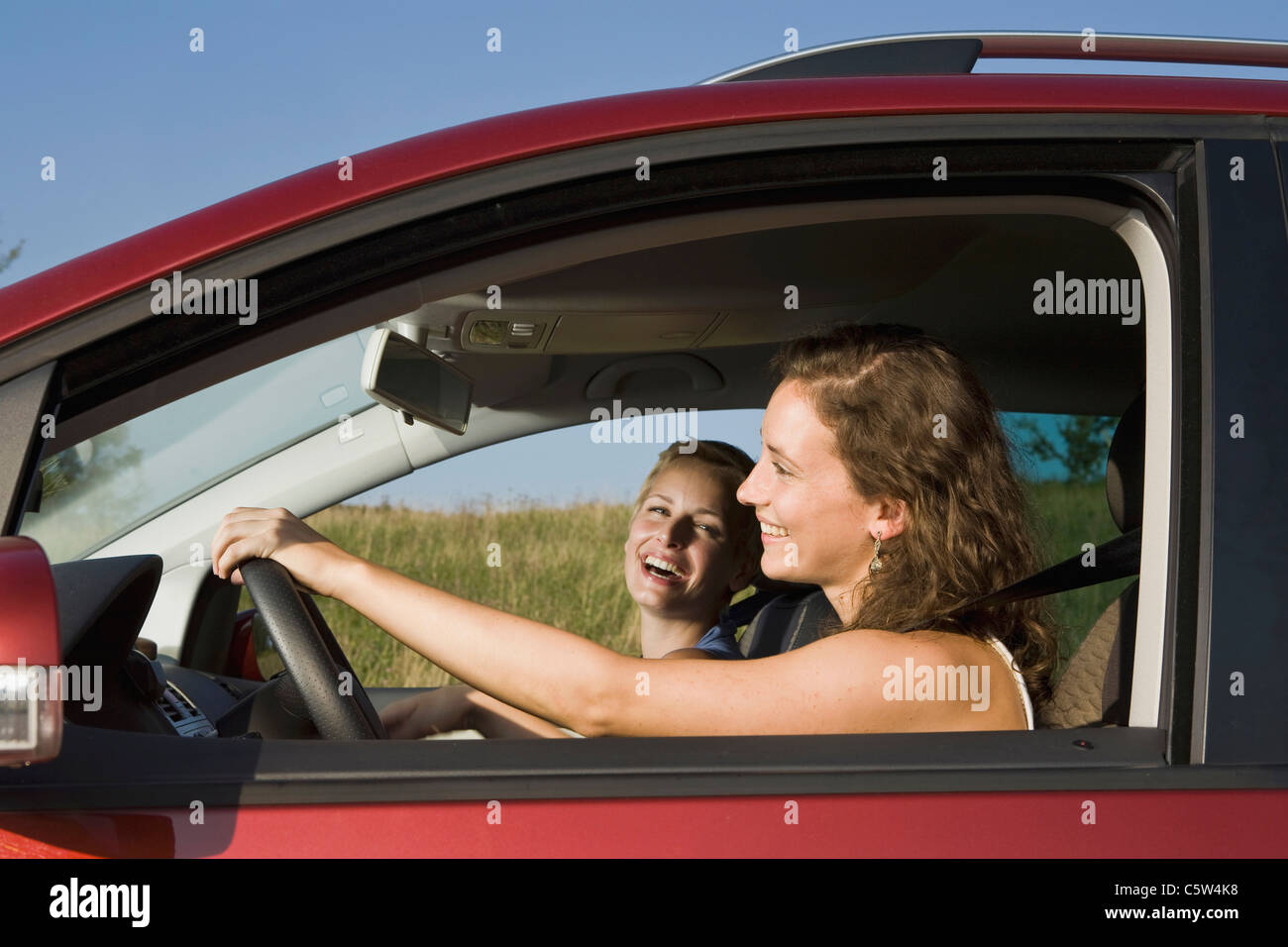 Germany, Bavaria, Two young women driving car, side view, portrait ...