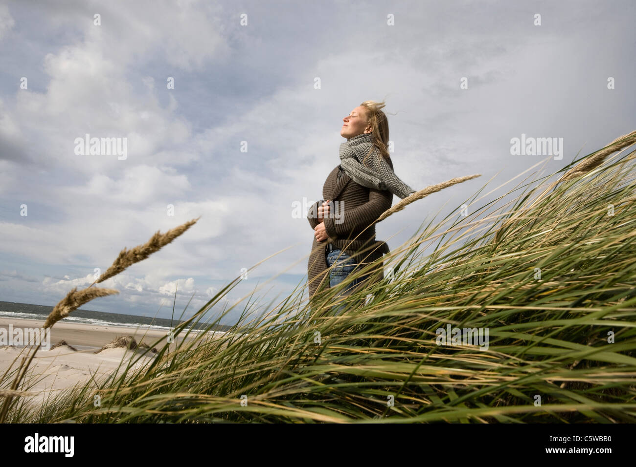 Germany, Schleswig Holstein, Amrum, Young woman on grassy sand dune ...