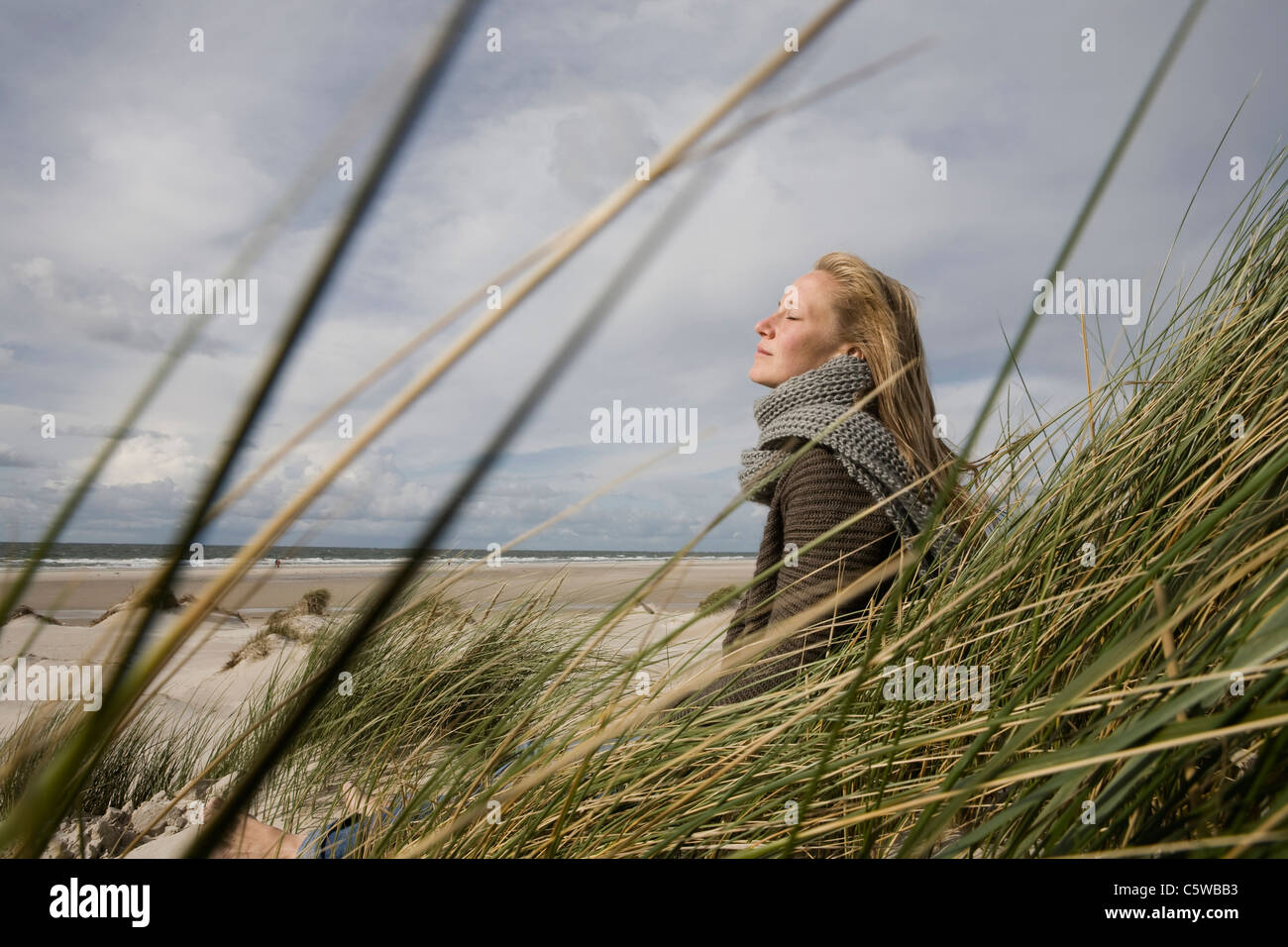 Germany, Schleswig Holstein, Amrum, Young woman on grassy sand dune ...