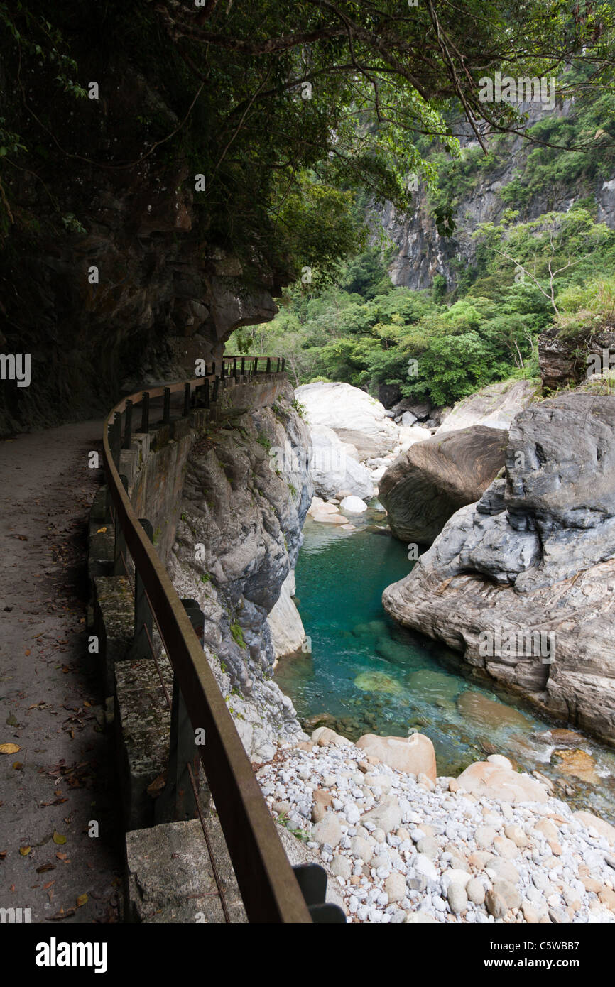 Cliffside trail under rock overhang and crystal clear stream flowing ...