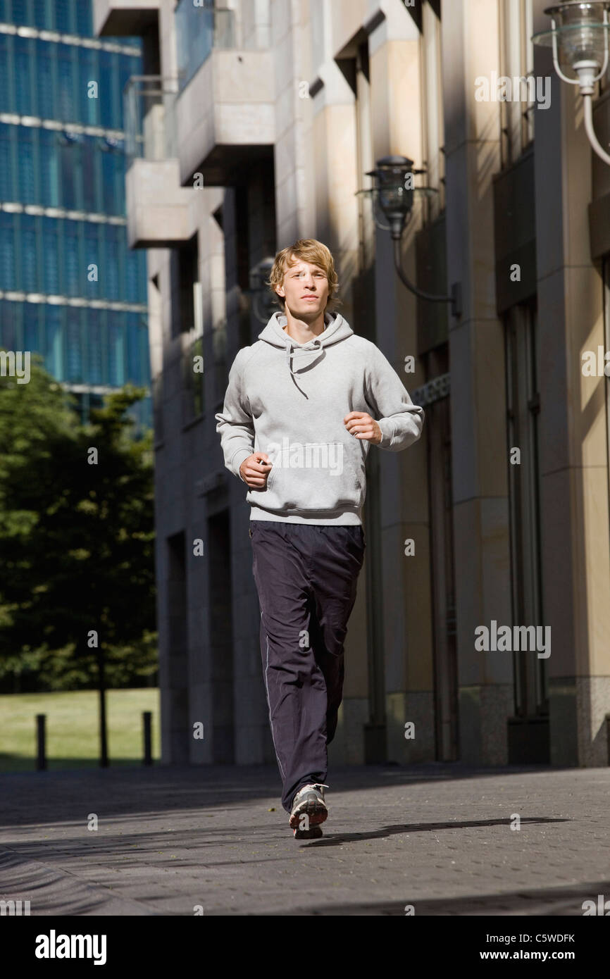 Germany, Berlin, Young man jogging in street, buildings in background ...