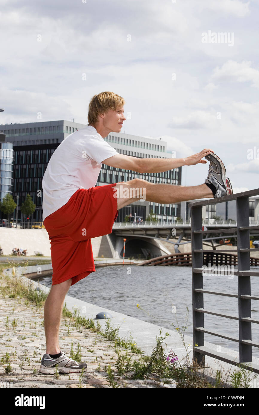 Germany, Berlin, Young man stretching leg on railing Stock Photo - Alamy