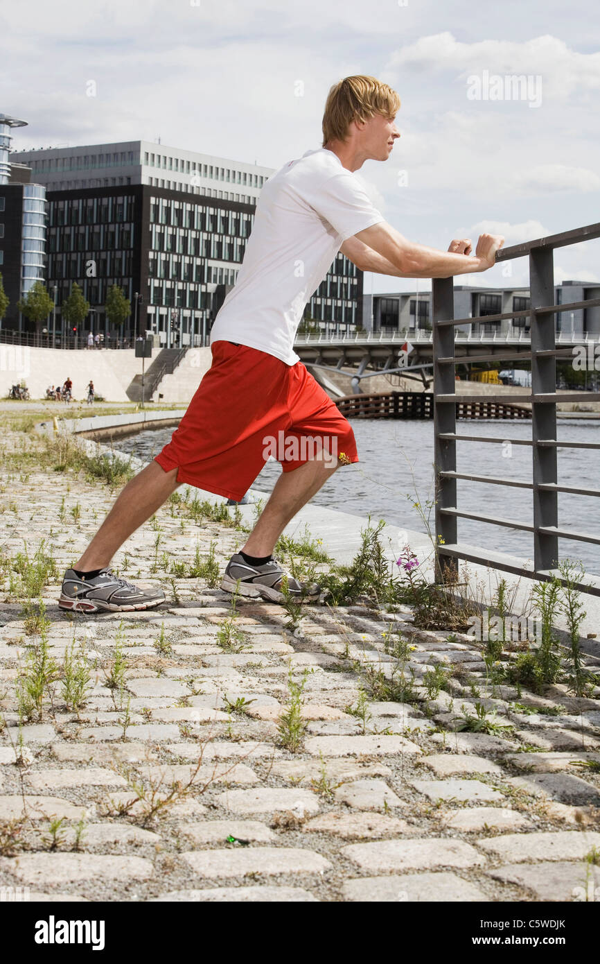 Germany, Berlin, Young man stretching on railing Stock Photo - Alamy