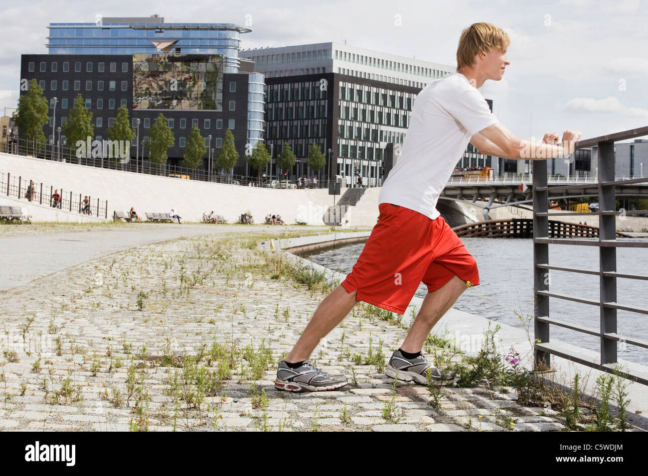 Germany, Berlin, Young man stretching on railing Stock Photo - Alamy