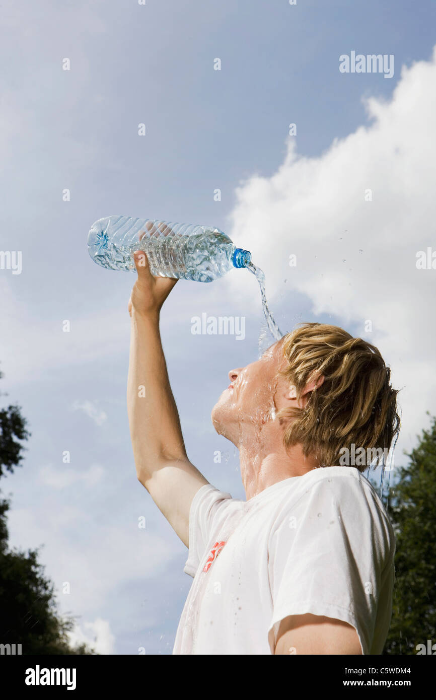 Germany, Berlin, Young man pouring water over face, side view, portrait ...