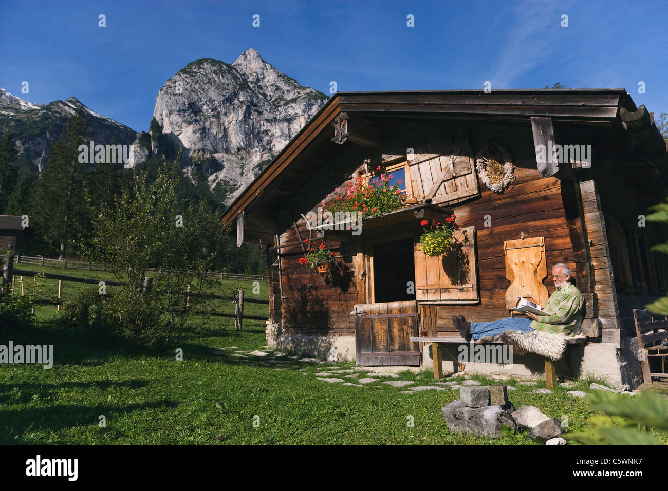 Austria, Karwendel, Senior man sitting in front of log cabin, reading a ...