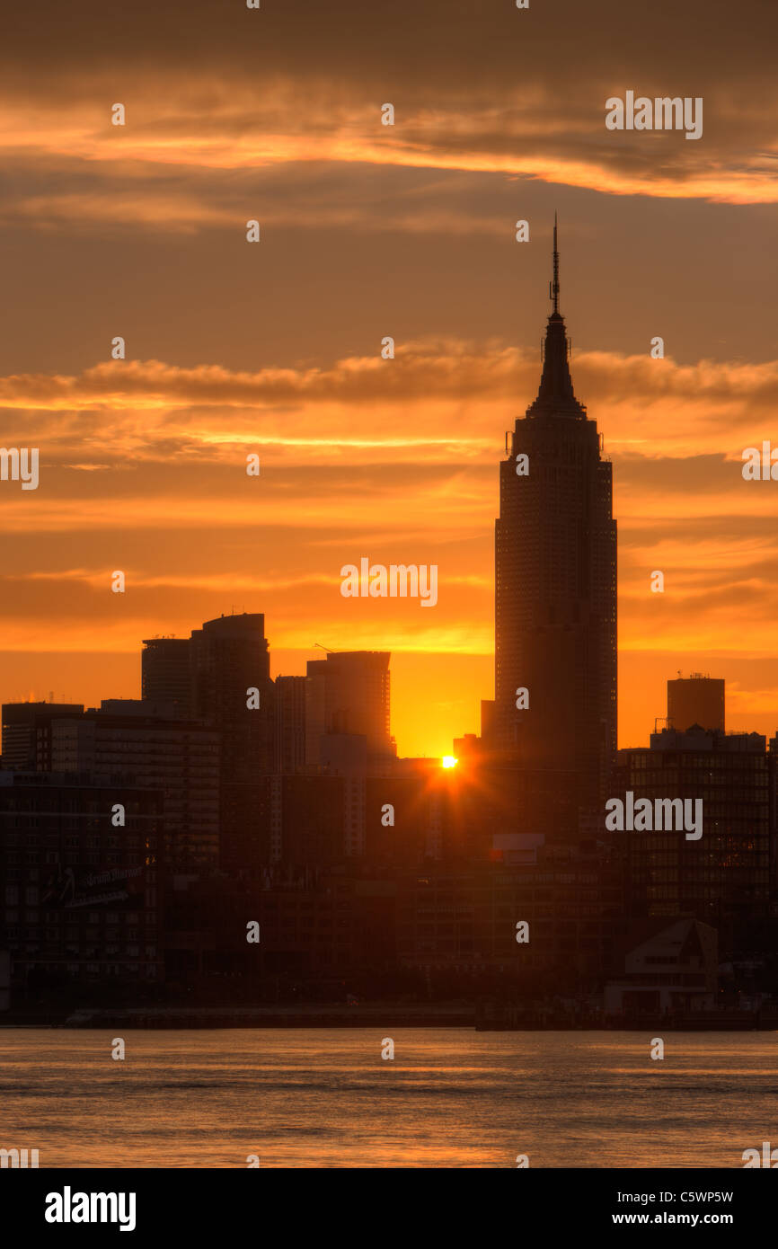 The rising sun shines between Manhattan buildings including the Empire ...