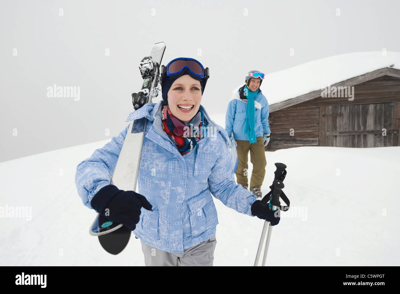 Italy, South Tyrol, Young couple, woman carrying skis over shoulder ...