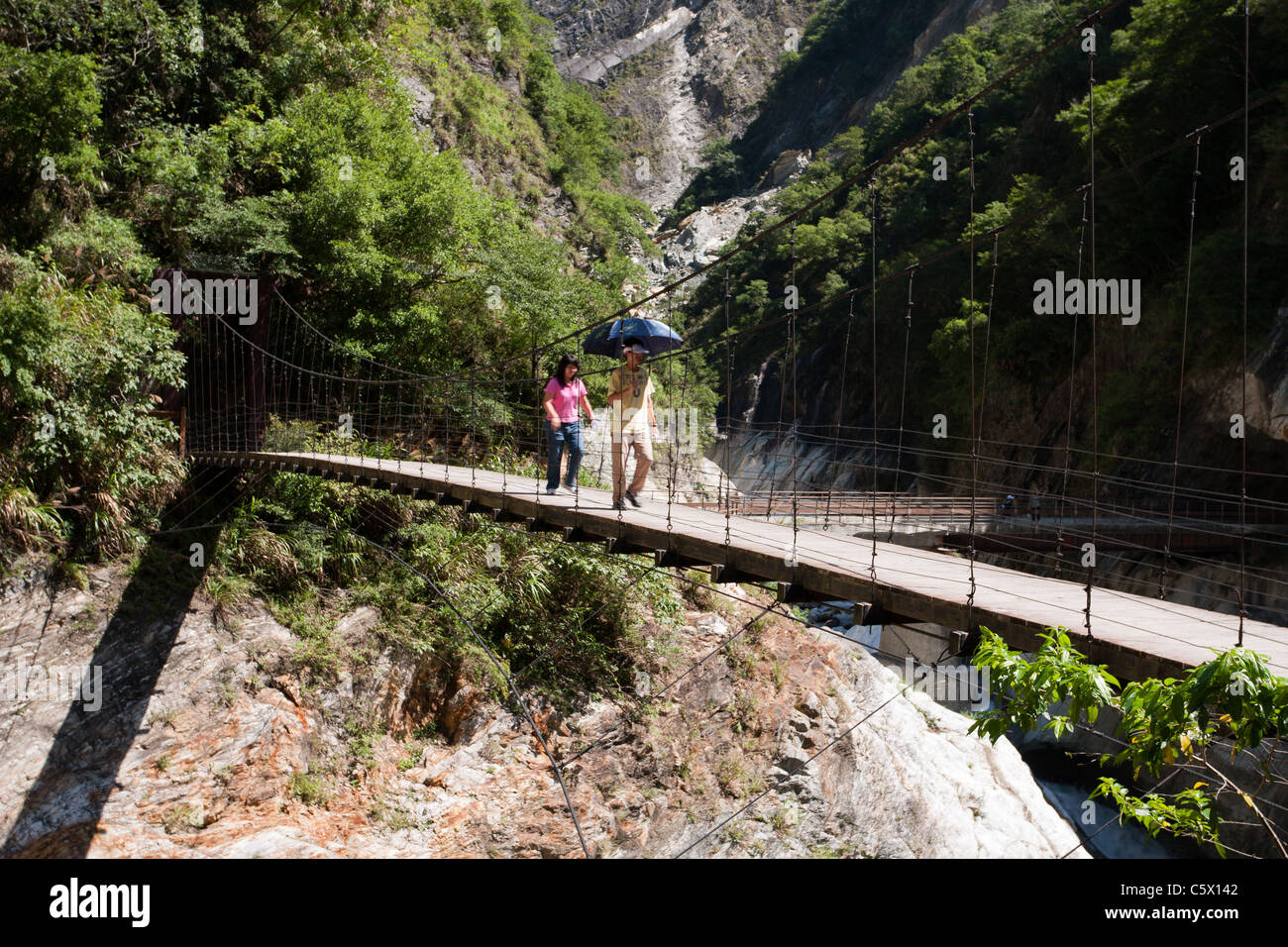 People walk through Baiyang Suspension Bridge, footbridge along marble ...