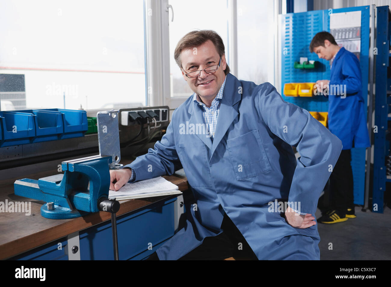 Germany, Neukirch, Man sitting at work bench, Apprentice in background ...