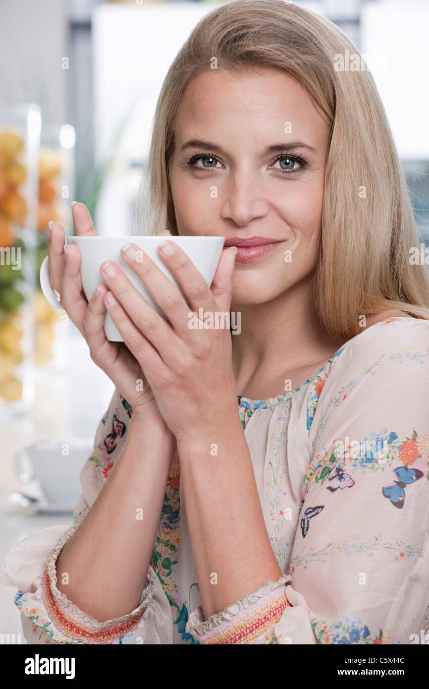 Germany, Cologne, Young woman in cafe holding a cup of coffee, portrait ...