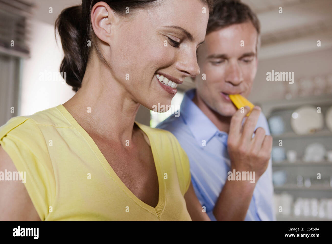 Germany, Hamburg, Couple in kitchen, man eating a piece of bell pepper ...