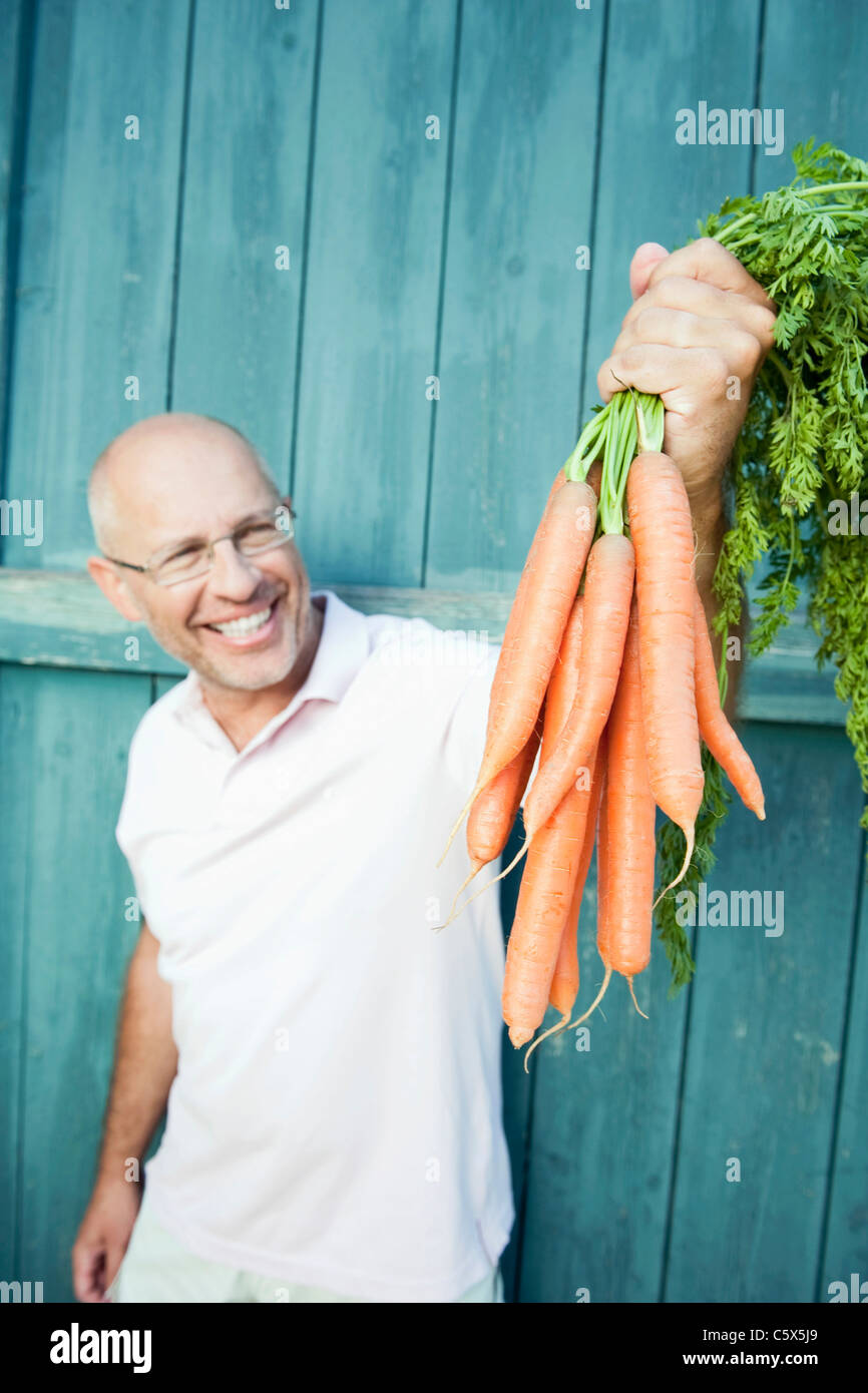 Germany, Bavaria, Man in front of barn door holding bunch of carrots ...