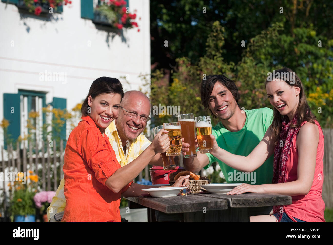 Germany, Bavaria, Friends drinking beer in the garden, clinking glasses ...