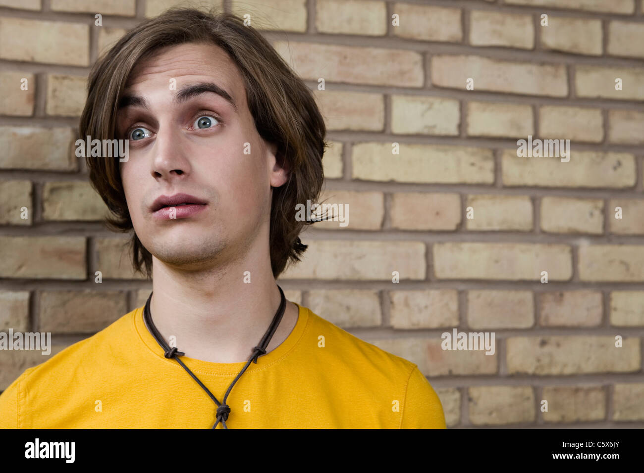 Germany, Berlin, Young man in front of brick wall looking shocked ...
