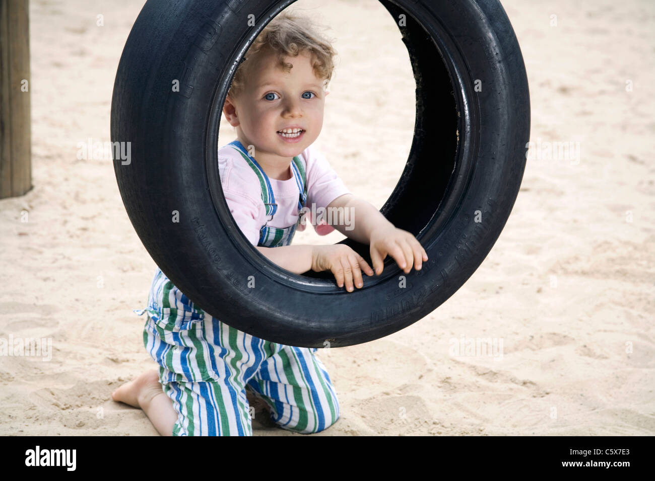 Germany, Berlin, Boy (3-4) looking through car tire at playground ...