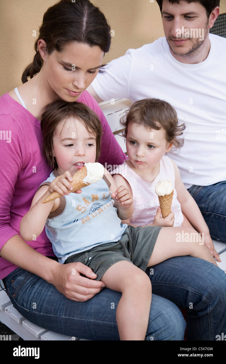 Germany, Berlin, Family sitting on bench, children (3-4) eating ...
