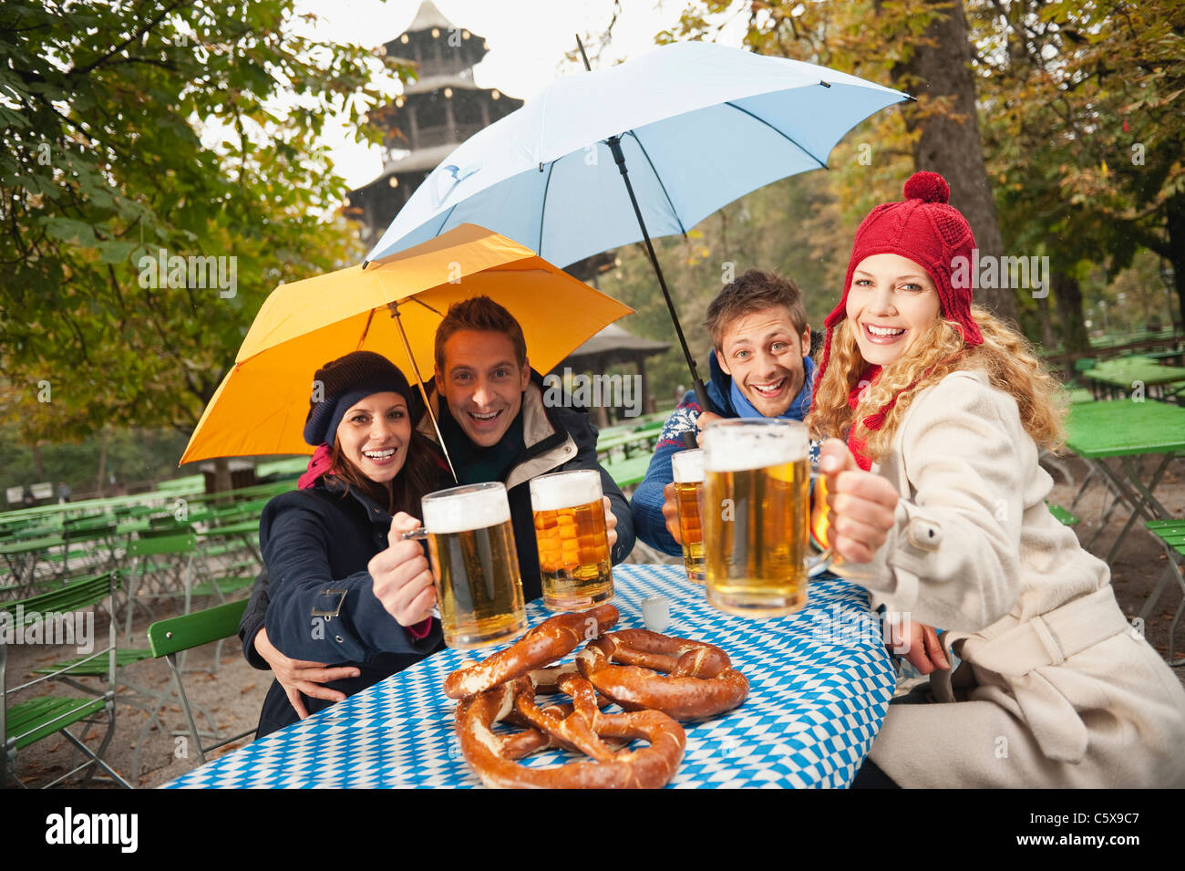 Germany, Bavaria, English Garden, Four persons sitting in rainy beer ...