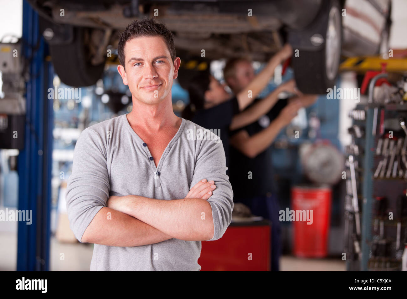 Portrait of a male mechanic looking at the camera with workers in the ...