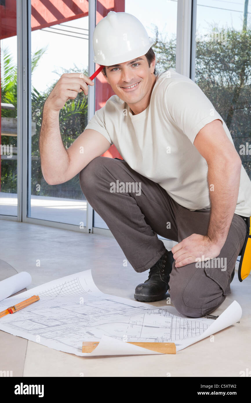 Smart young construction worker smiling with blueprint on floor Stock ...
