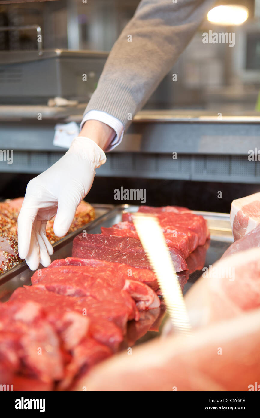 A butcher's hand reaching into a cooler picking a fresh cut of meat ...