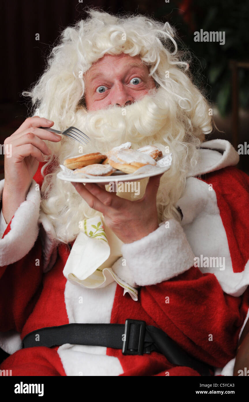 Crazy-eyed smiling Father Christmas holding a fork about to eat a plate ...