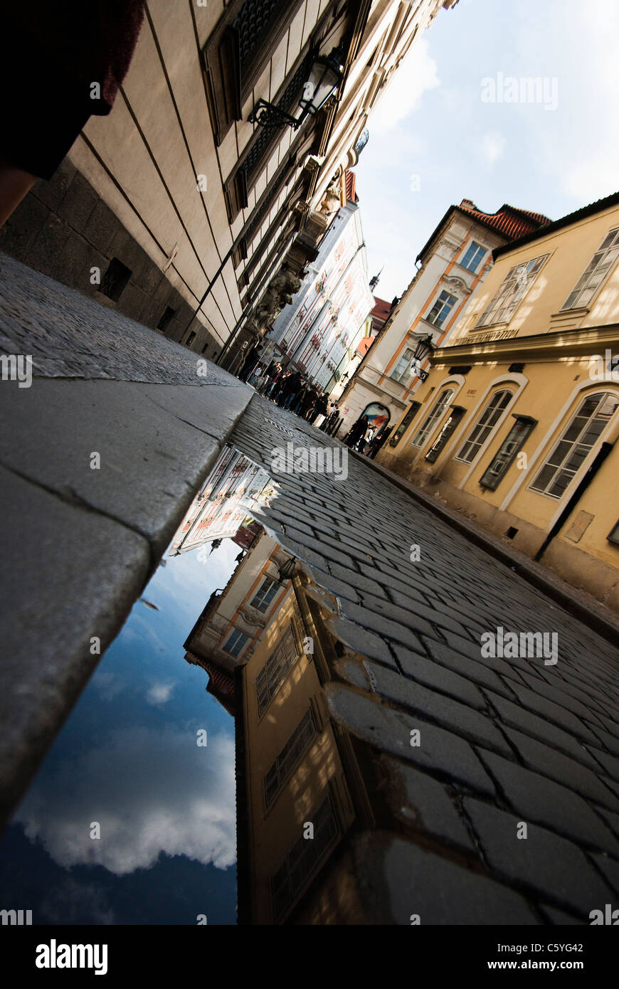 cobblestone street in prague with reflection of buildings in a puddle ...