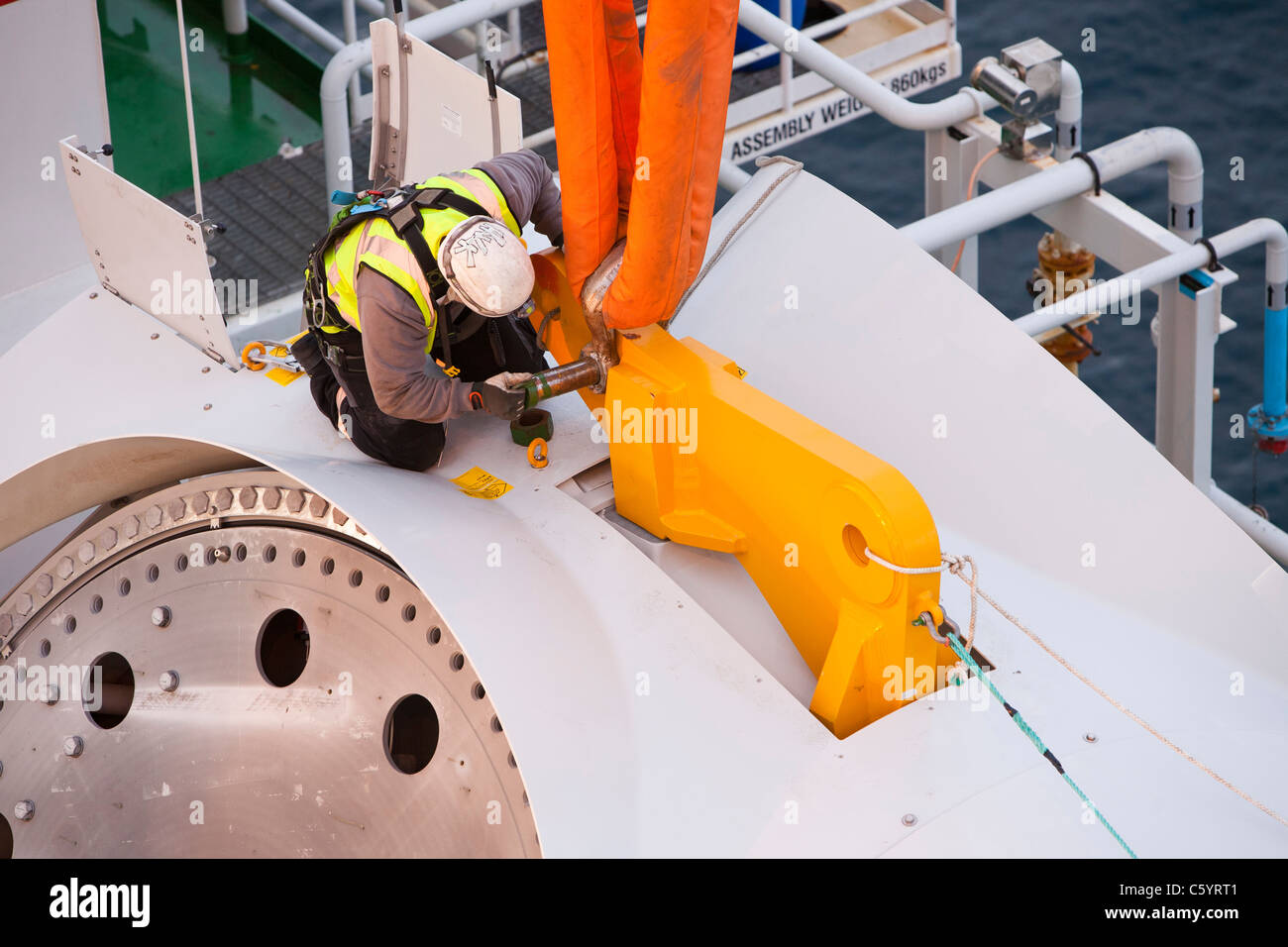 Workers prepare to lift a wind turbine nose cone on the jack up barge ...