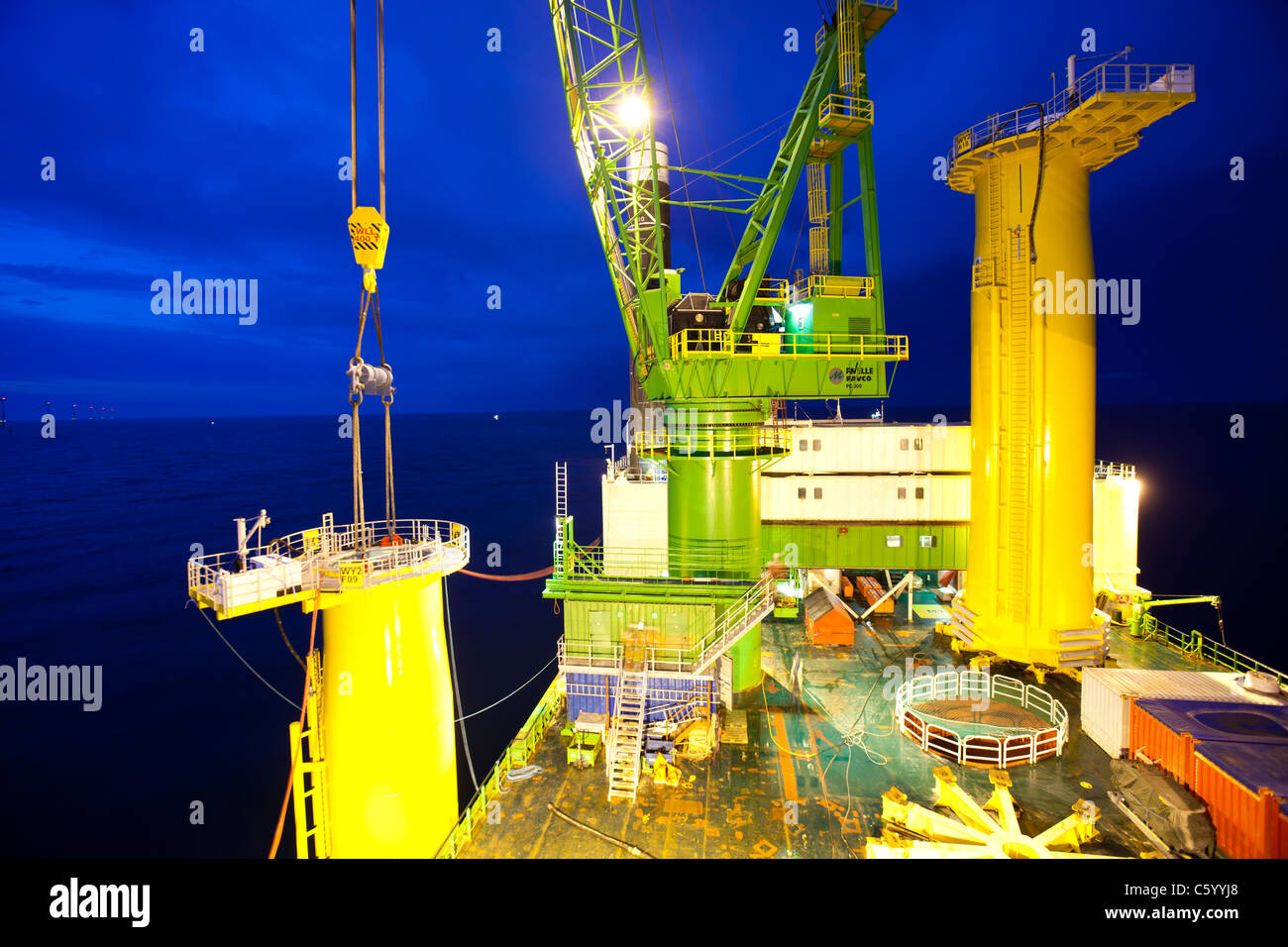 A crane lifts a transition piece into place at dawn on the Walney ...