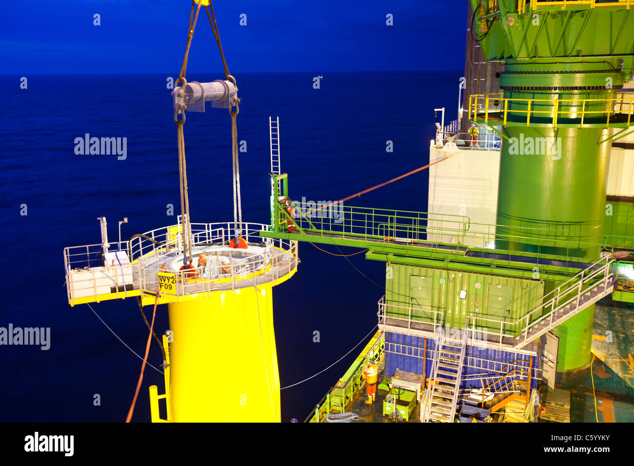 A crane lifts a transition piece into place at dawn on the Walney ...