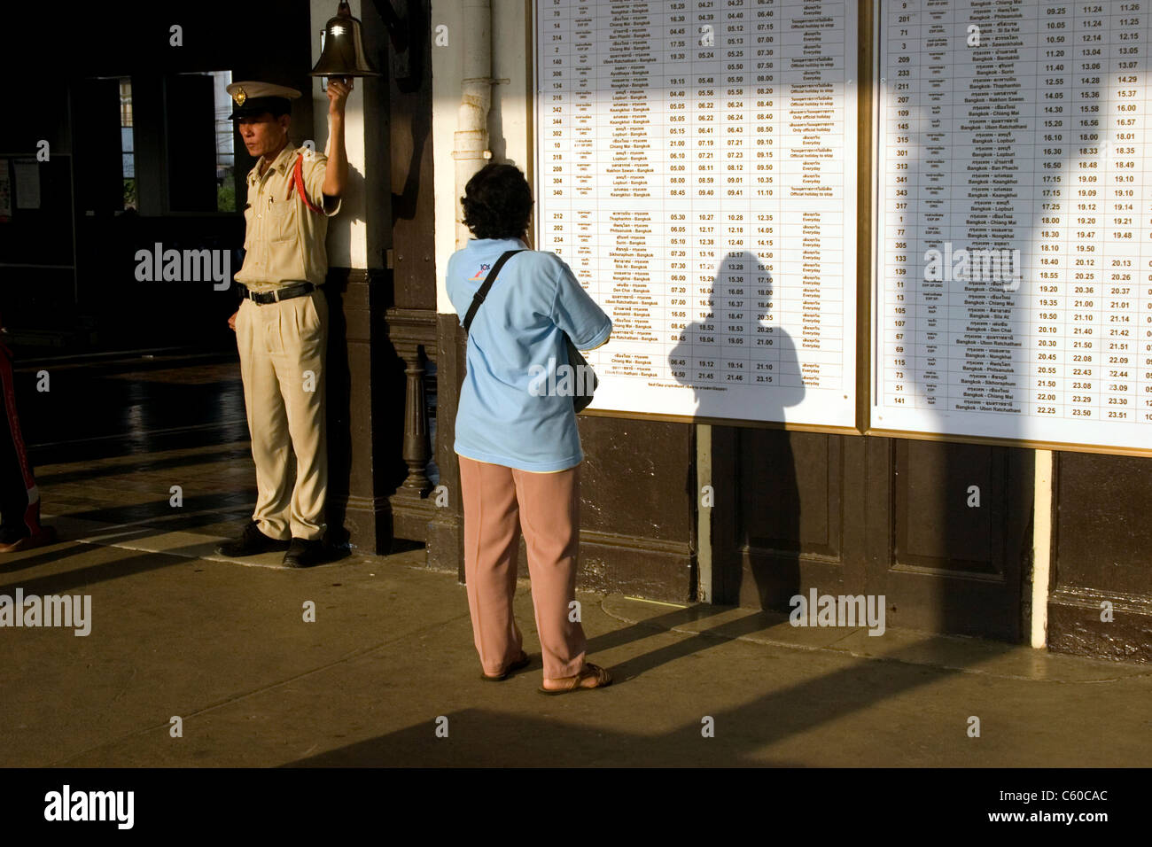 A woman is reading a schedule board and a railroad employee is ringing ...