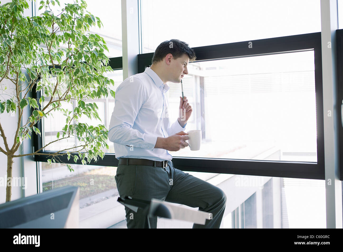 Businessman peering out office window Stock Photo - Alamy
