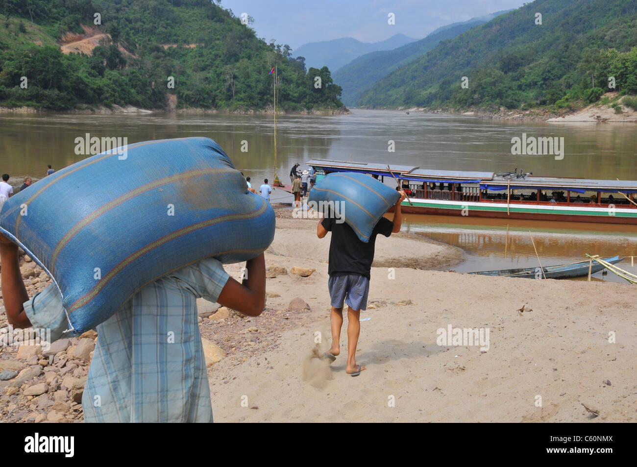young boys carrying heavy sack of rice Mekong river Laos Stock Photo ...
