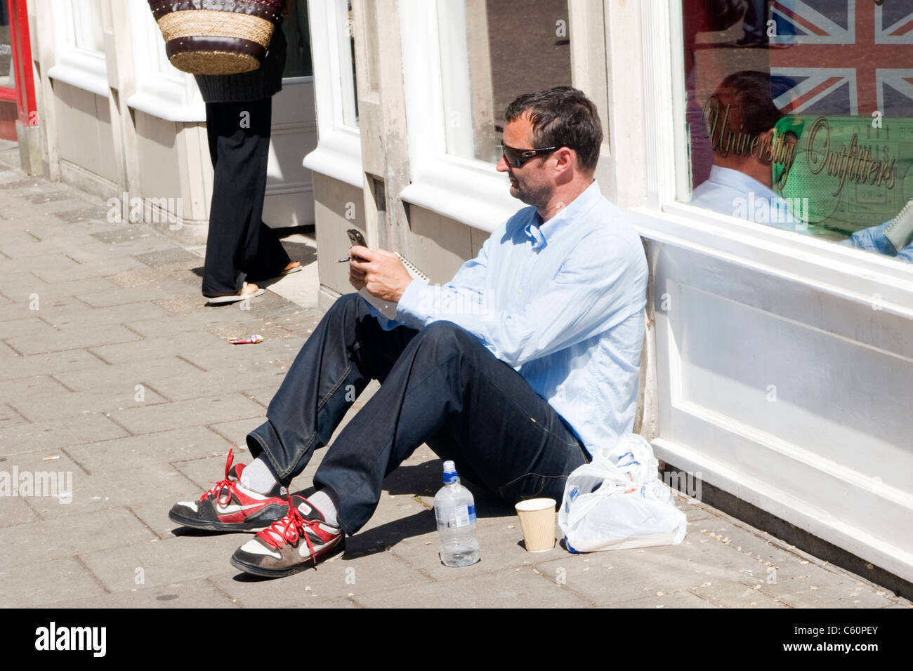 Brighton East Sussex man checks iPhone seated on pavement with drink of ...