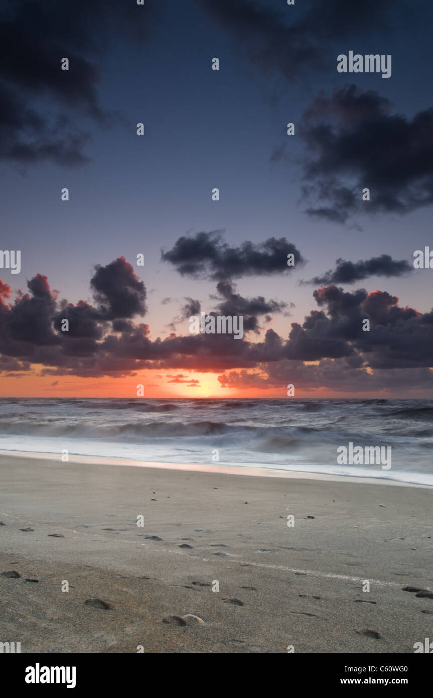 A beach during sunset with glowing sky with dark clouds Stock Photo - Alamy
