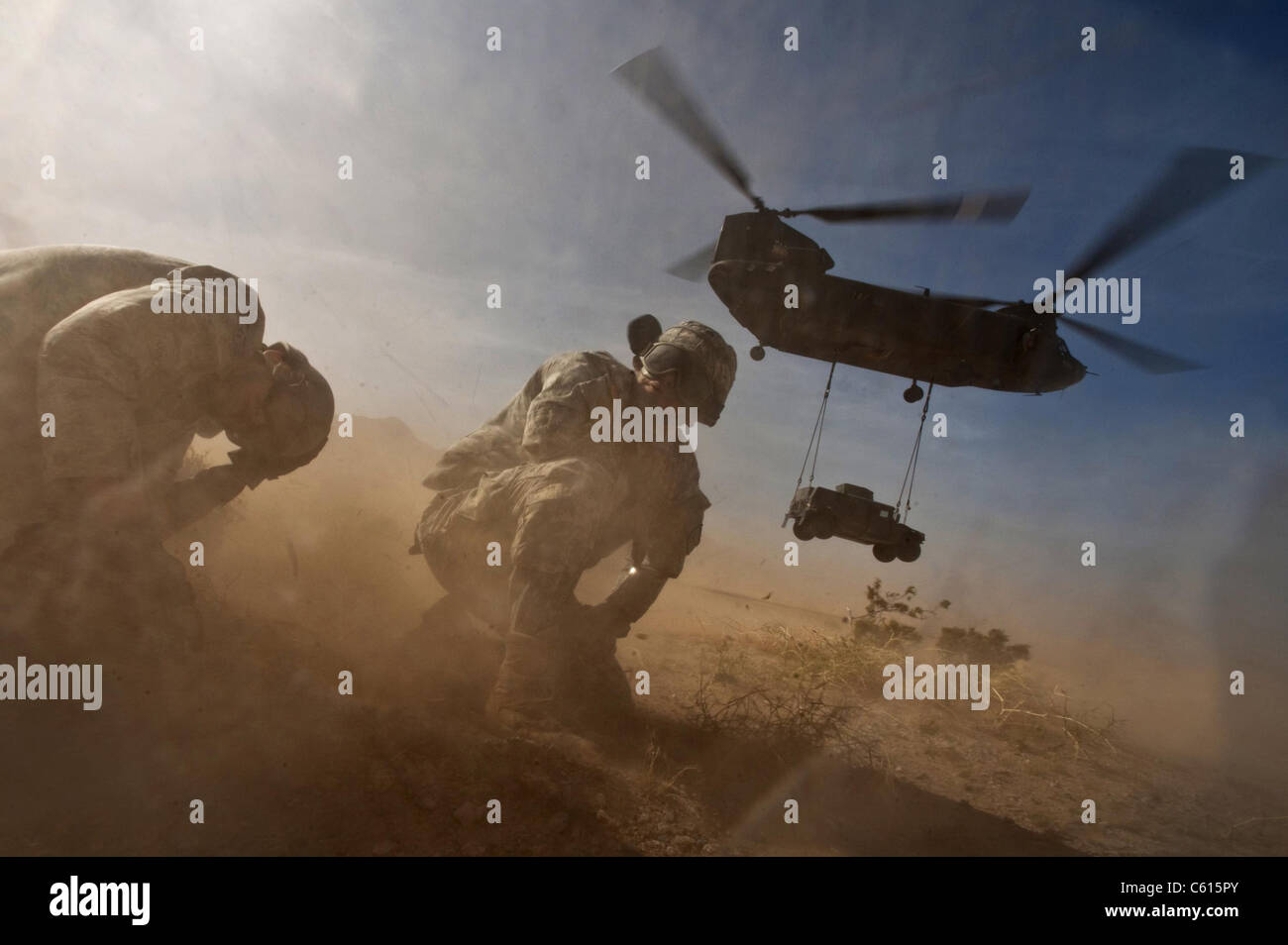 Soldiers in the dust of a Chinook helicopter hauling a Humvee at Nellis ...