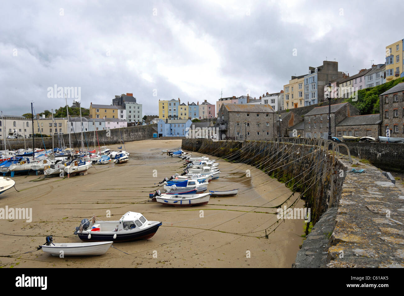 Small boats tied-up to the stone harbour sea defenses at Tenby in Wales ...