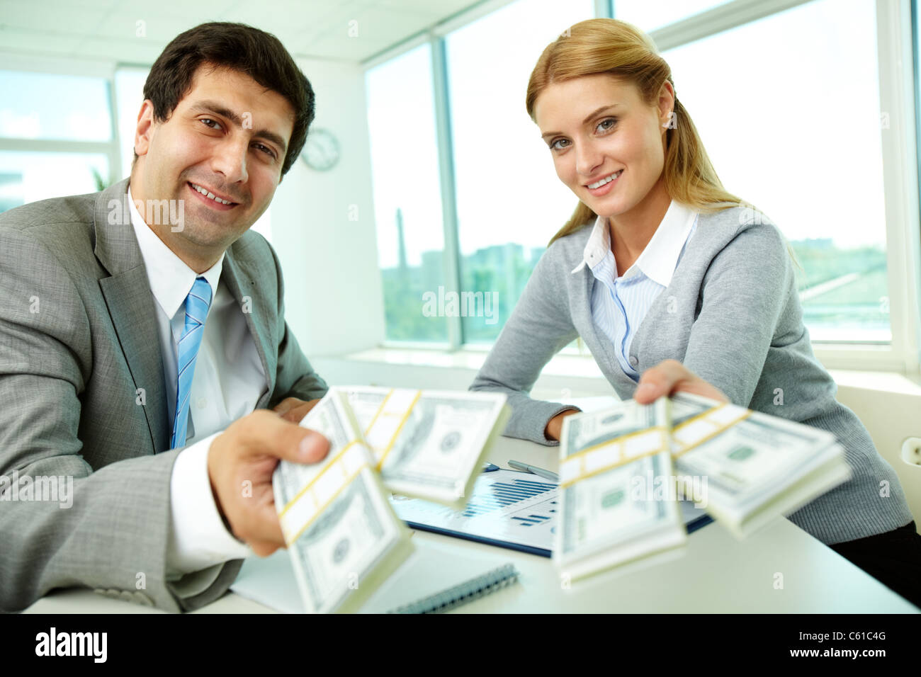 Two business partners at workplace giving money and looking at you ...