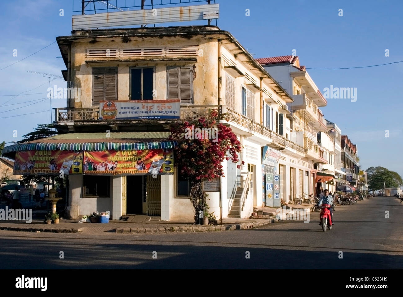 A man is riding a motorcycle past an old rundown building on a street ...