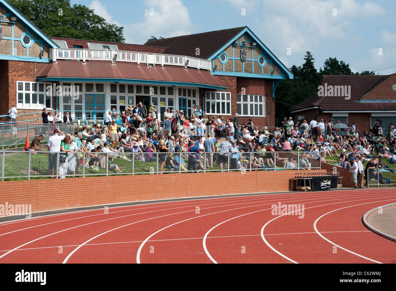 Spectators gathered alongside an athletics racing track on a sunny day ...