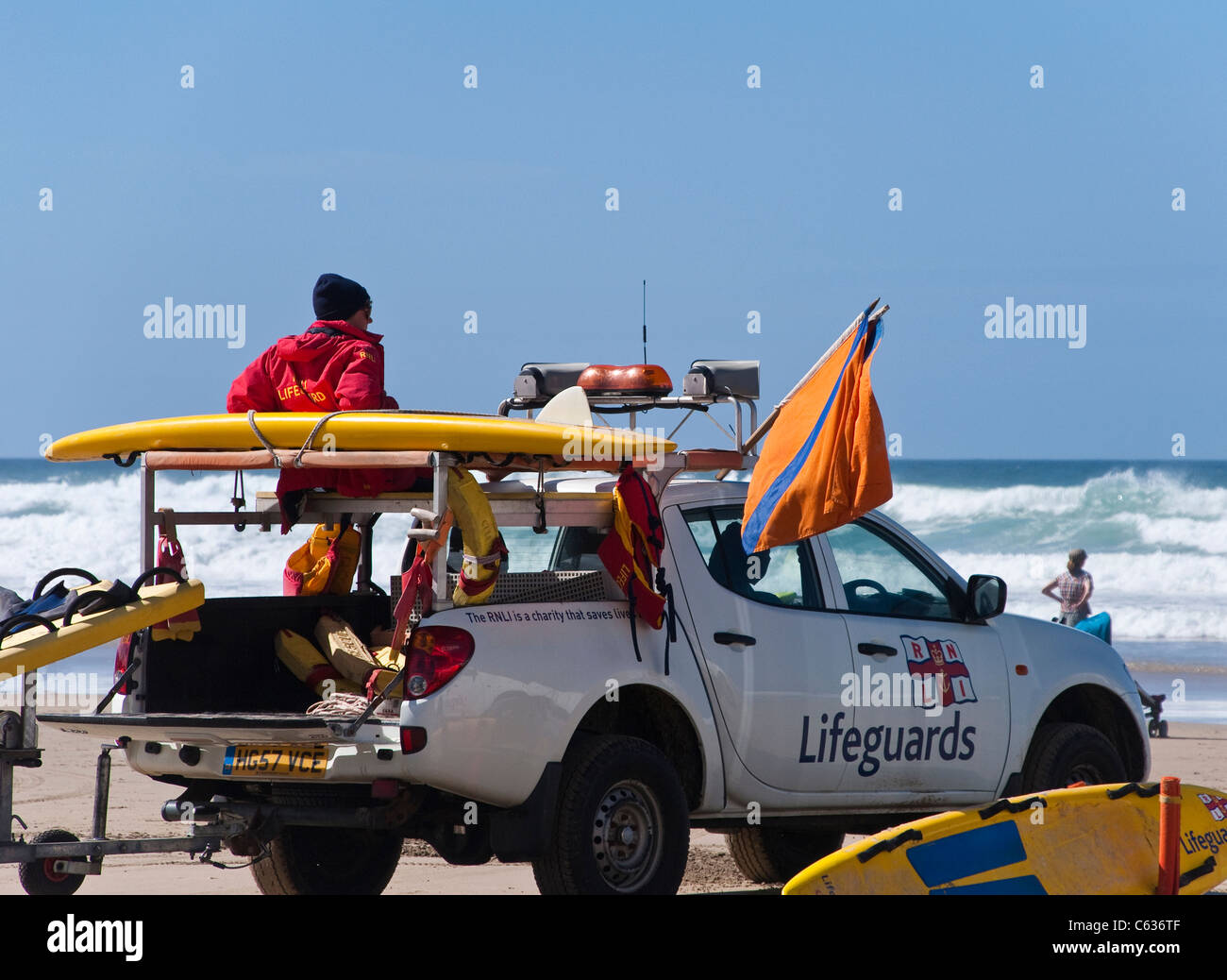 RNLI volunteer lifeguard on the beach at Perranporth, Cornwall, sitting ...