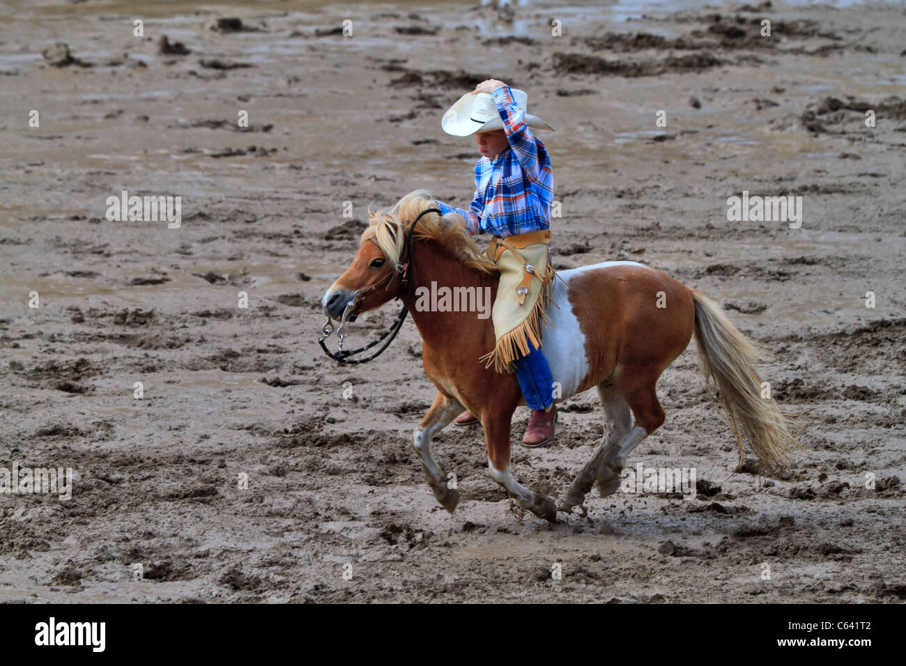The littlest cowboy. A little boy rides his pony in the muddy infield ...