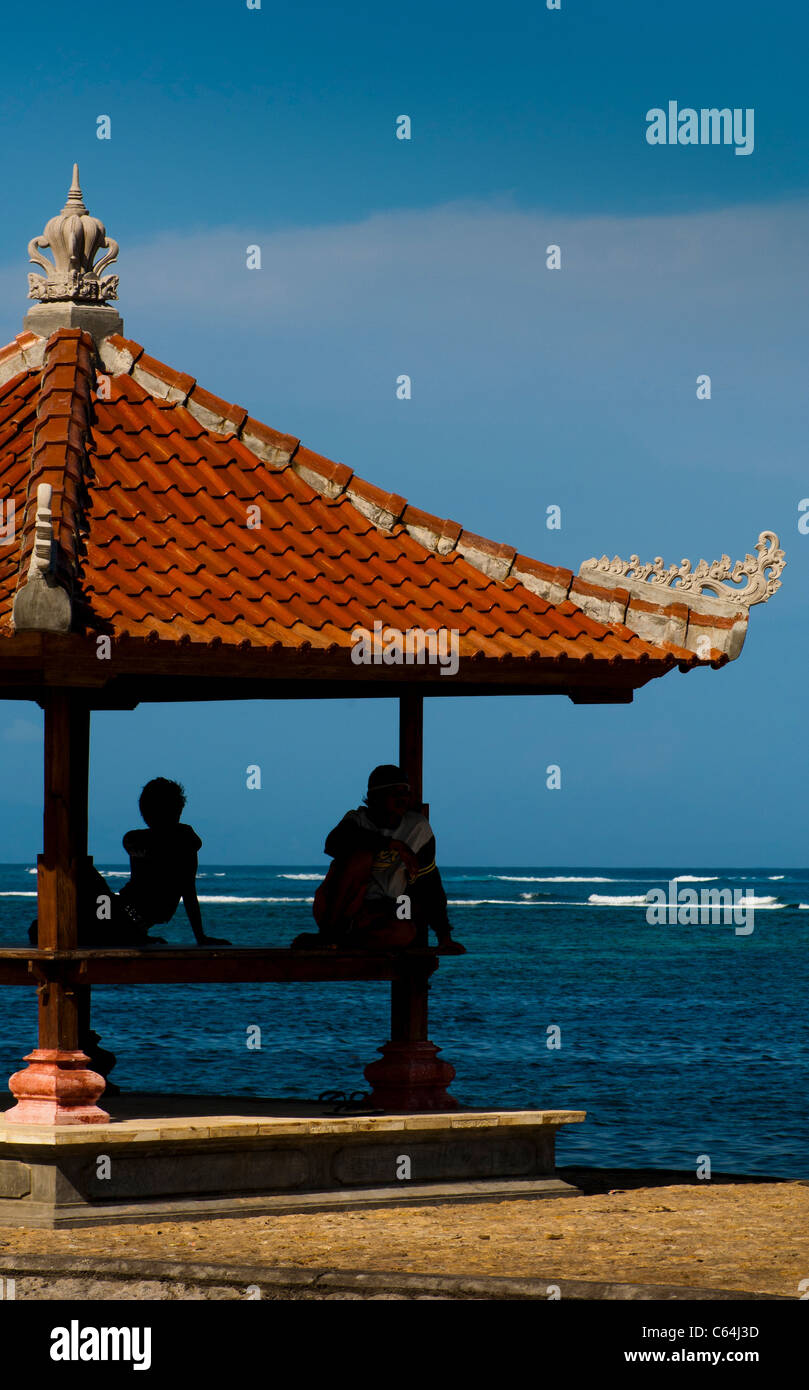 2 silhouetted people sitting in the shade of a Balinese bale hut, Nusa ...
