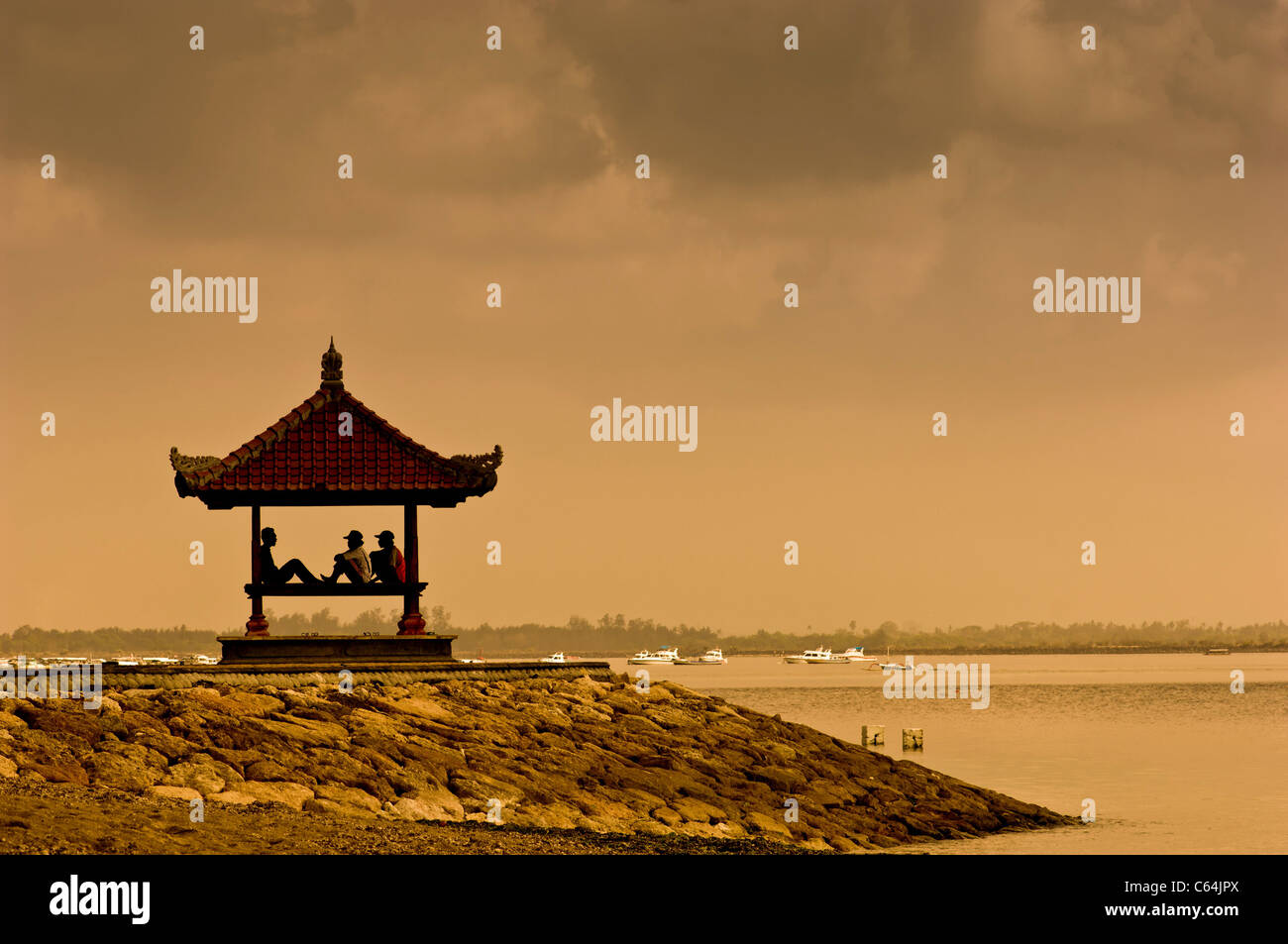 3 silhouetted males sitting in a Balinese bale hut on Nusa Dua Beach ...