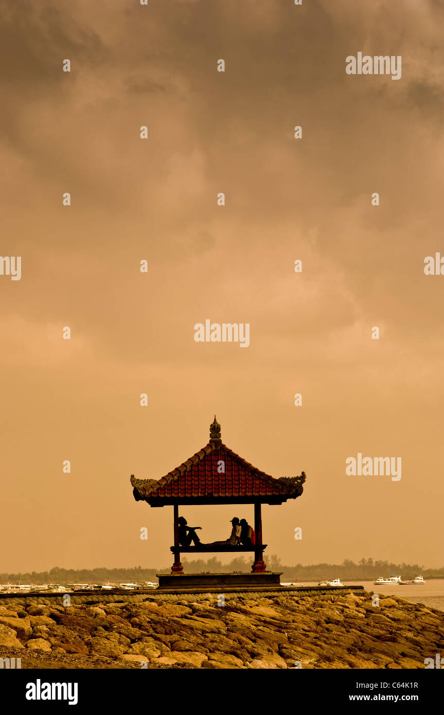 3 silhouetted males sitting in a Balinese bale hut on Nusa Dua Beach ...
