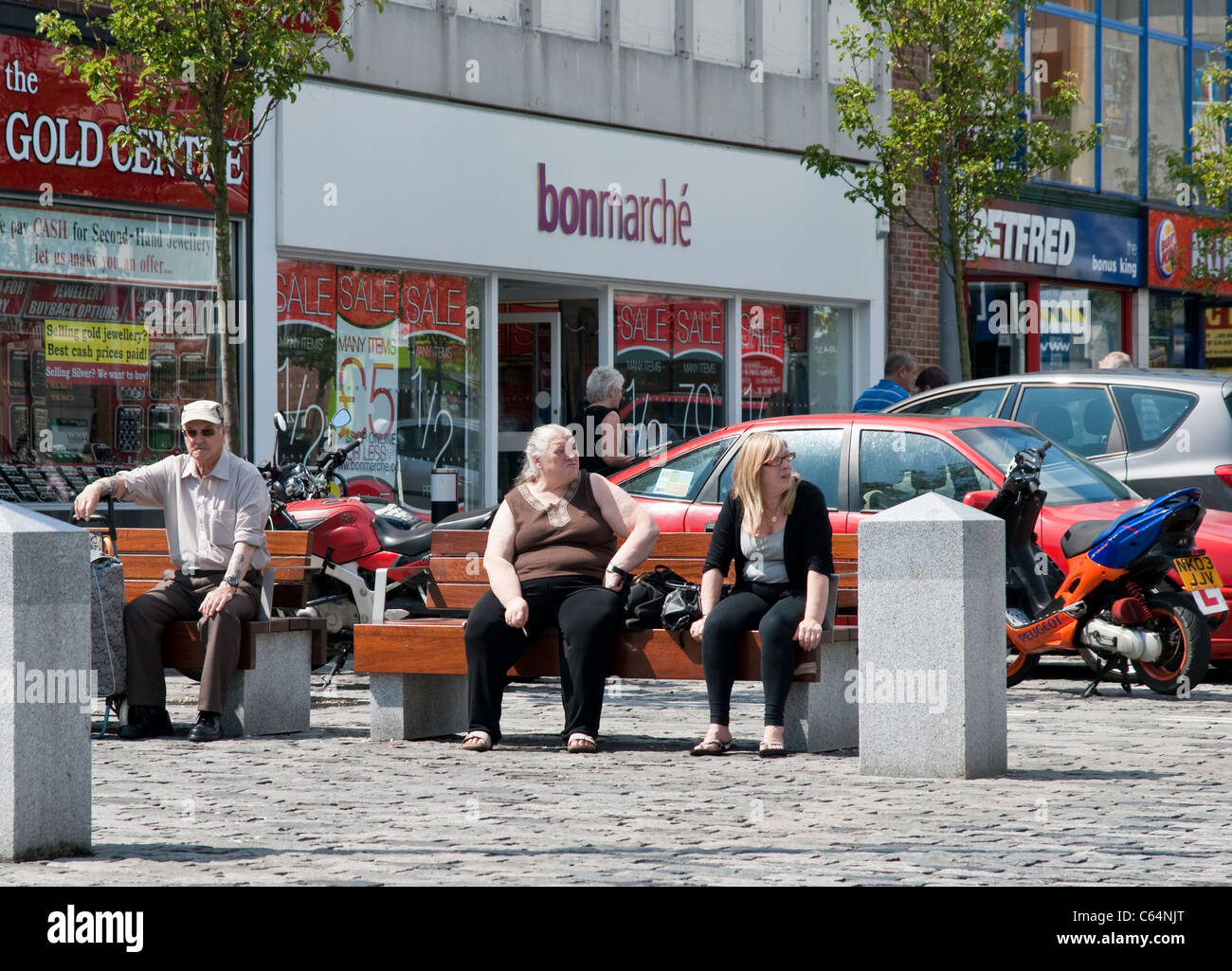A horizontal long shot of three people sitting on a bench in a city ...