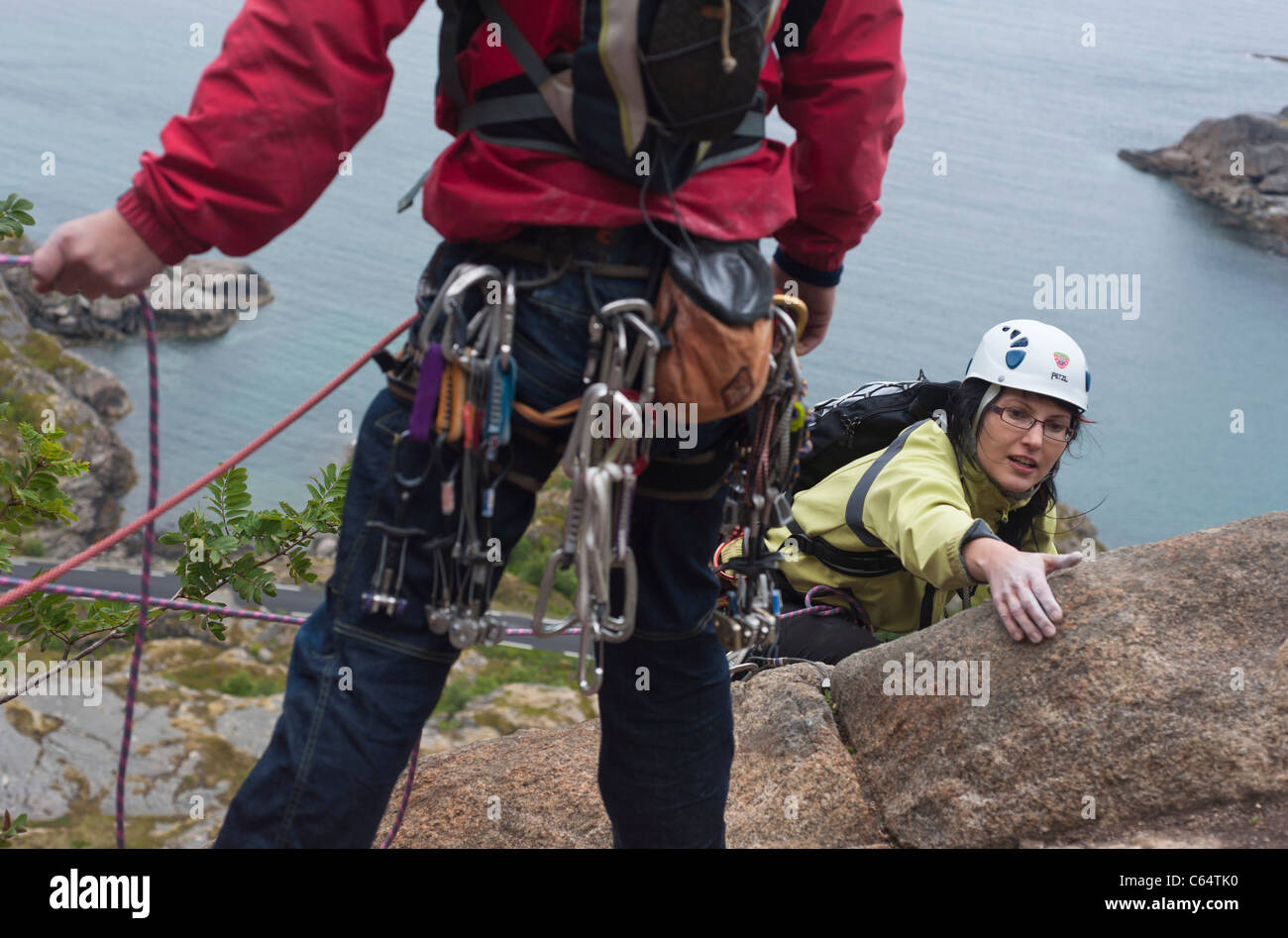 A male climber belaying a female climber as she climbs up a granite ...